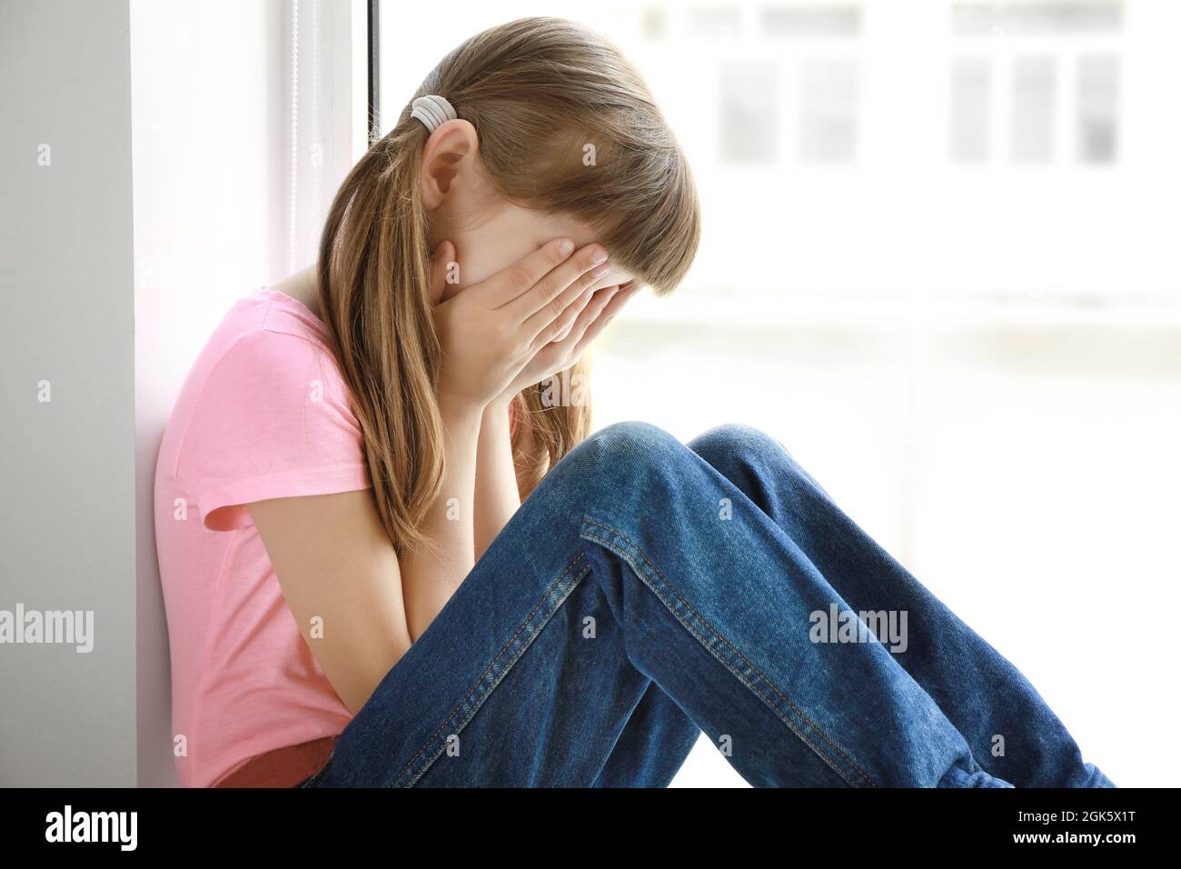 Sad little girl sitting on window sill at home Stock Photo - Alamy