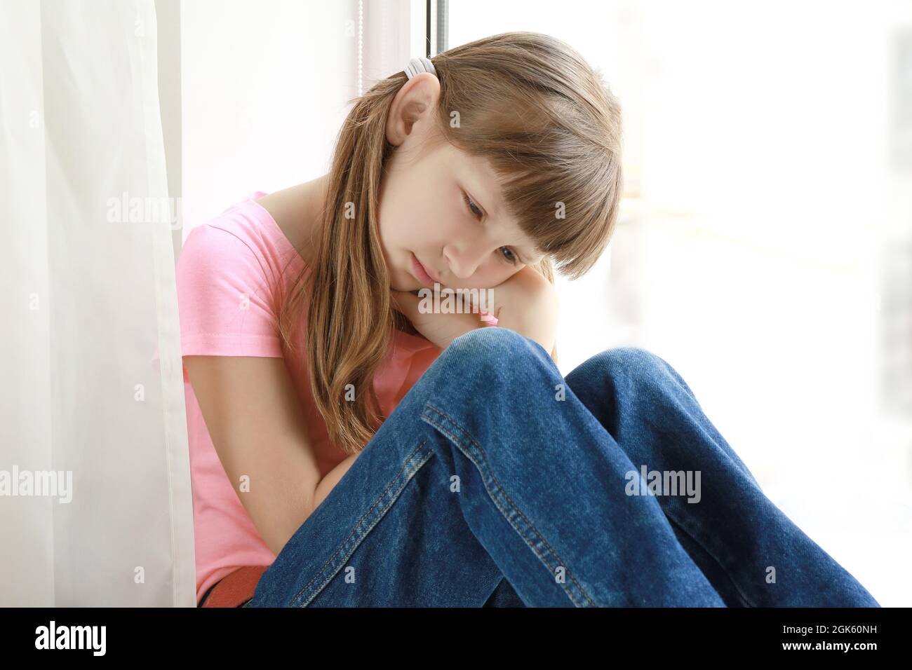Sad little girl sitting on window sill at home Stock Photo - Alamy