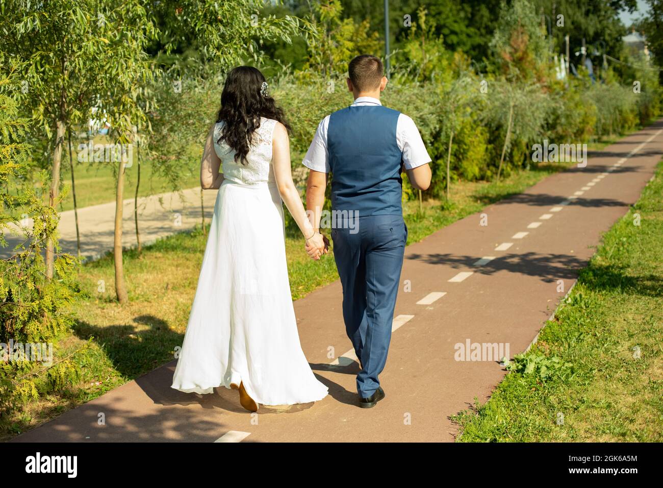 The newlyweds walk along the park path holding hands. A guy and a girl ...