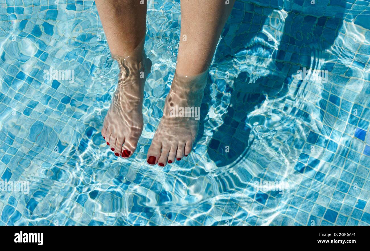 Woman's feet with red painted nails dipped in the water of a swimming ...