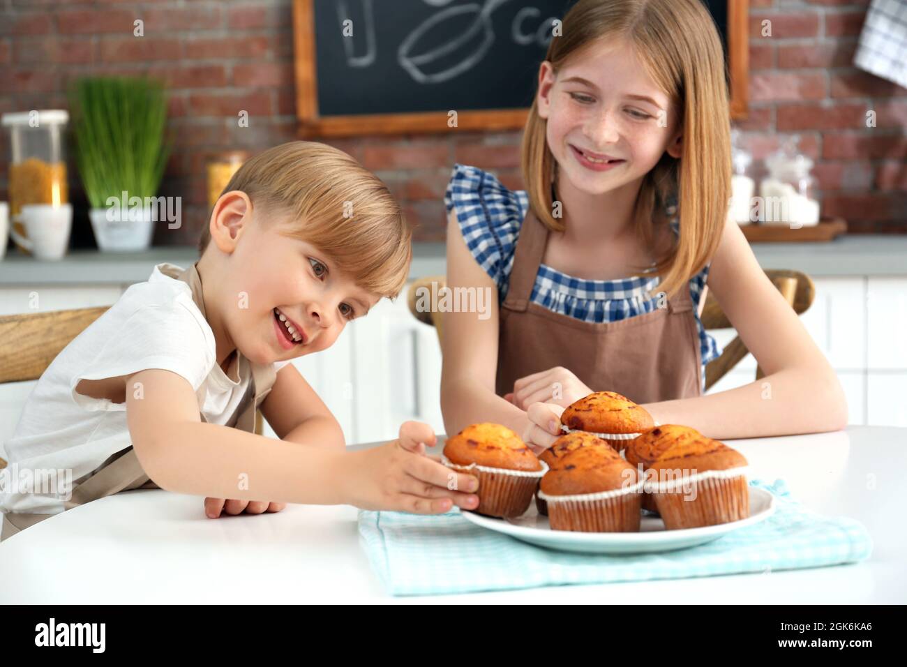 Boy and girl eating yummy muffins in kitchen. Cooking classes concept ...