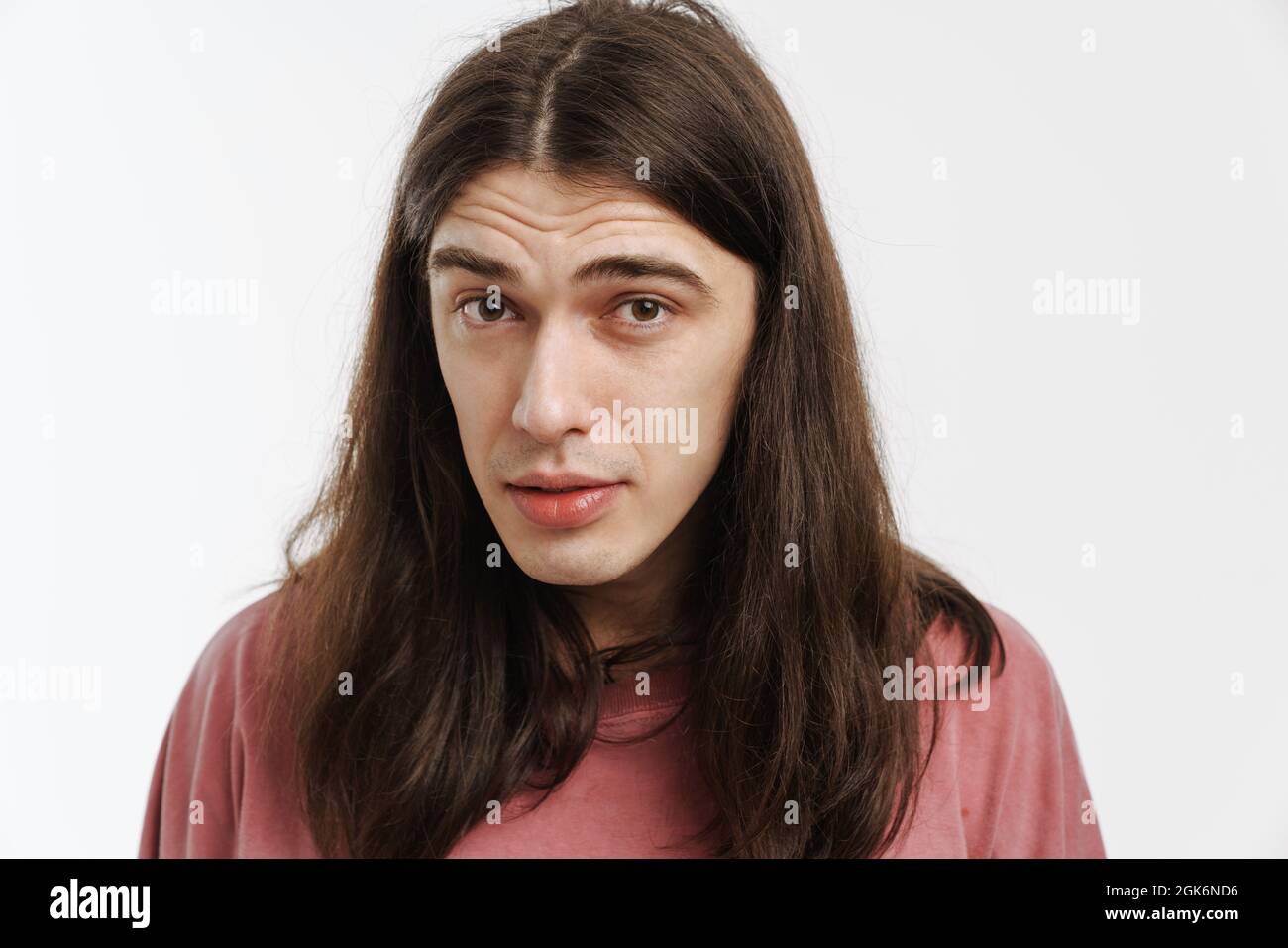 Young confused man with long hair posing and looking at camera isolated ...