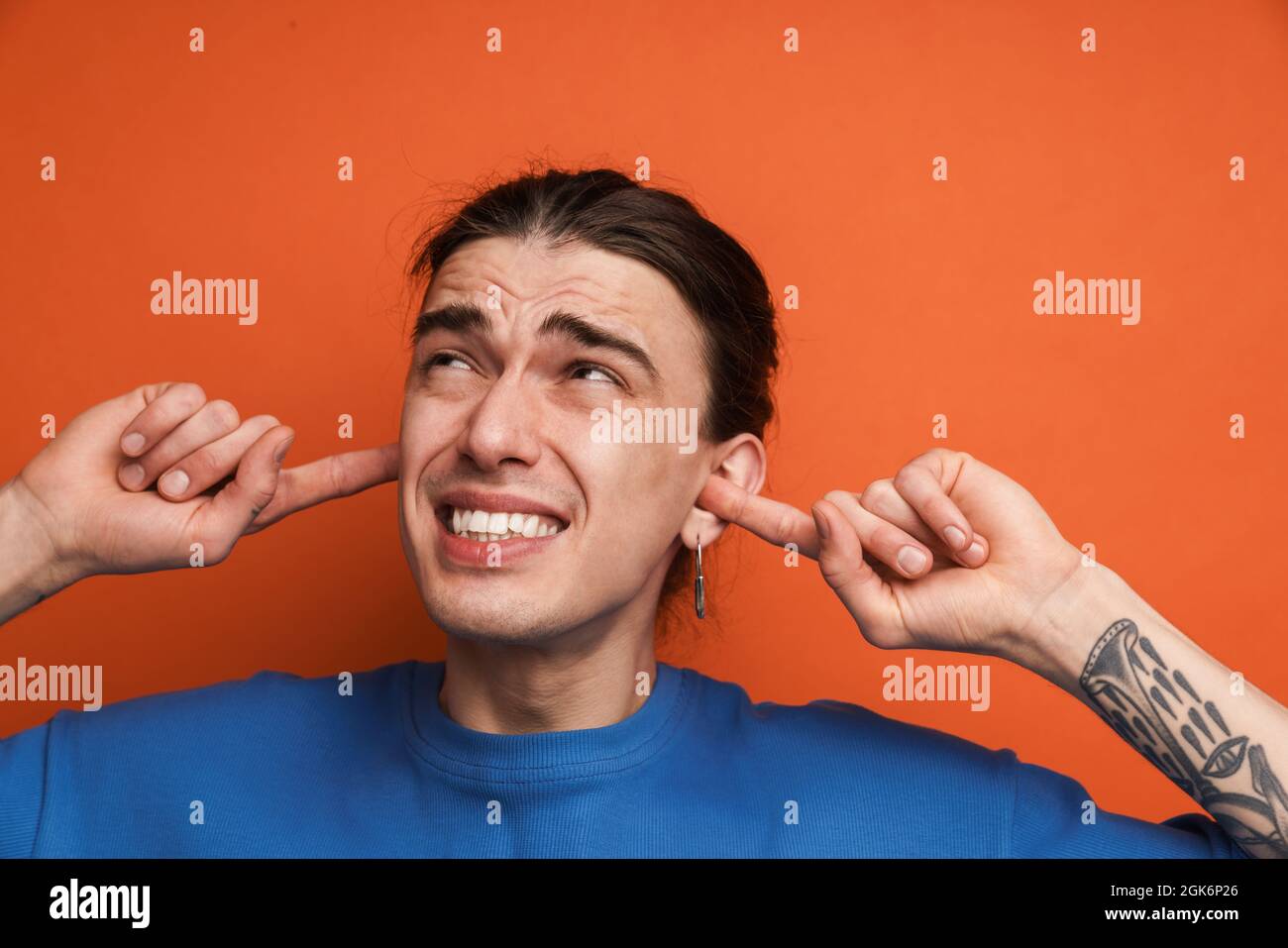 Young white man with earring frowning and plugging his ears isolated ...
