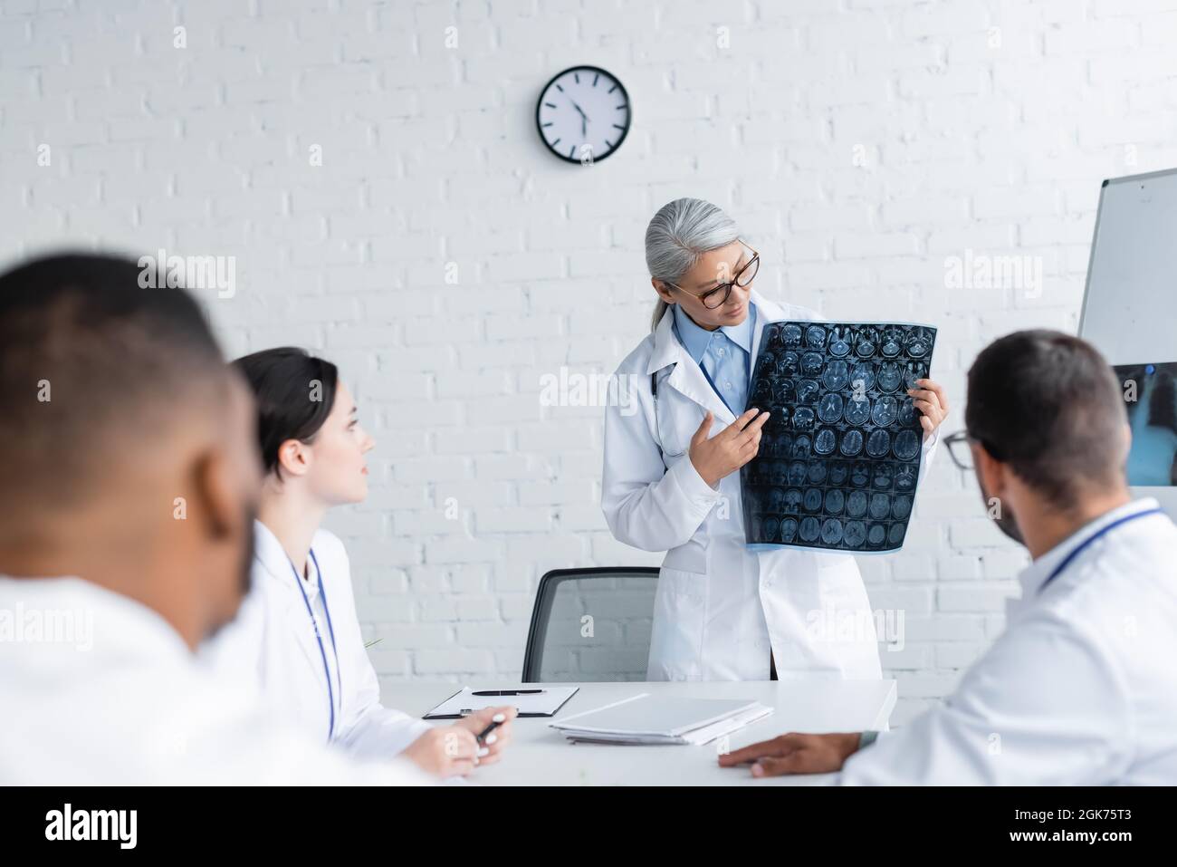 mature asian physician showing head mri scan to blurred multicultural ...