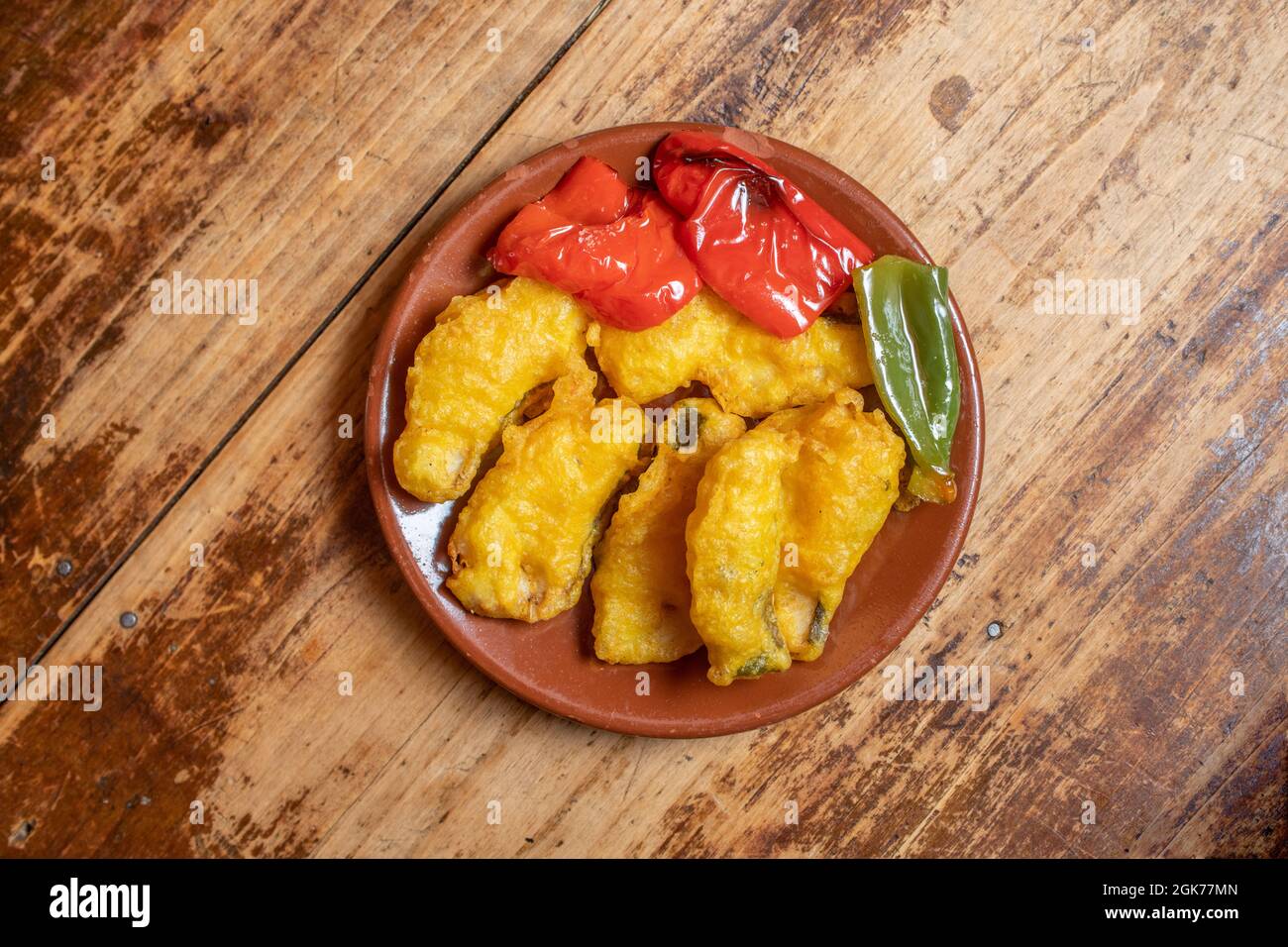 Top view of clay plate with battered cod portion and fried peppers as ...