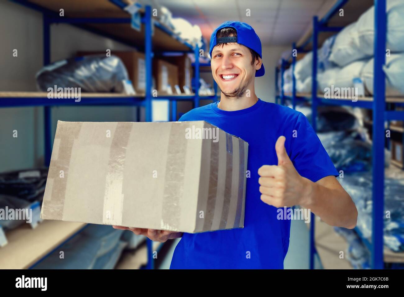 A young positive warehouse worker holds a cardboard box in his hands ...