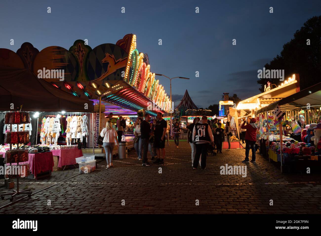 Outdoor night view of amusement park with crowd of visitors, colourful ...