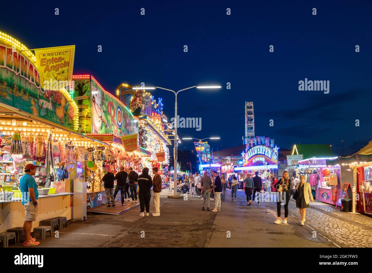 Outdoor night view of amusement park with crowd of visitors, colourful ...