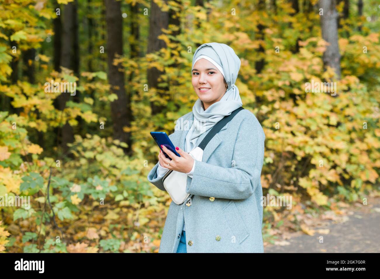 Islamic young woman wearing hijab standing on autumn park background ...