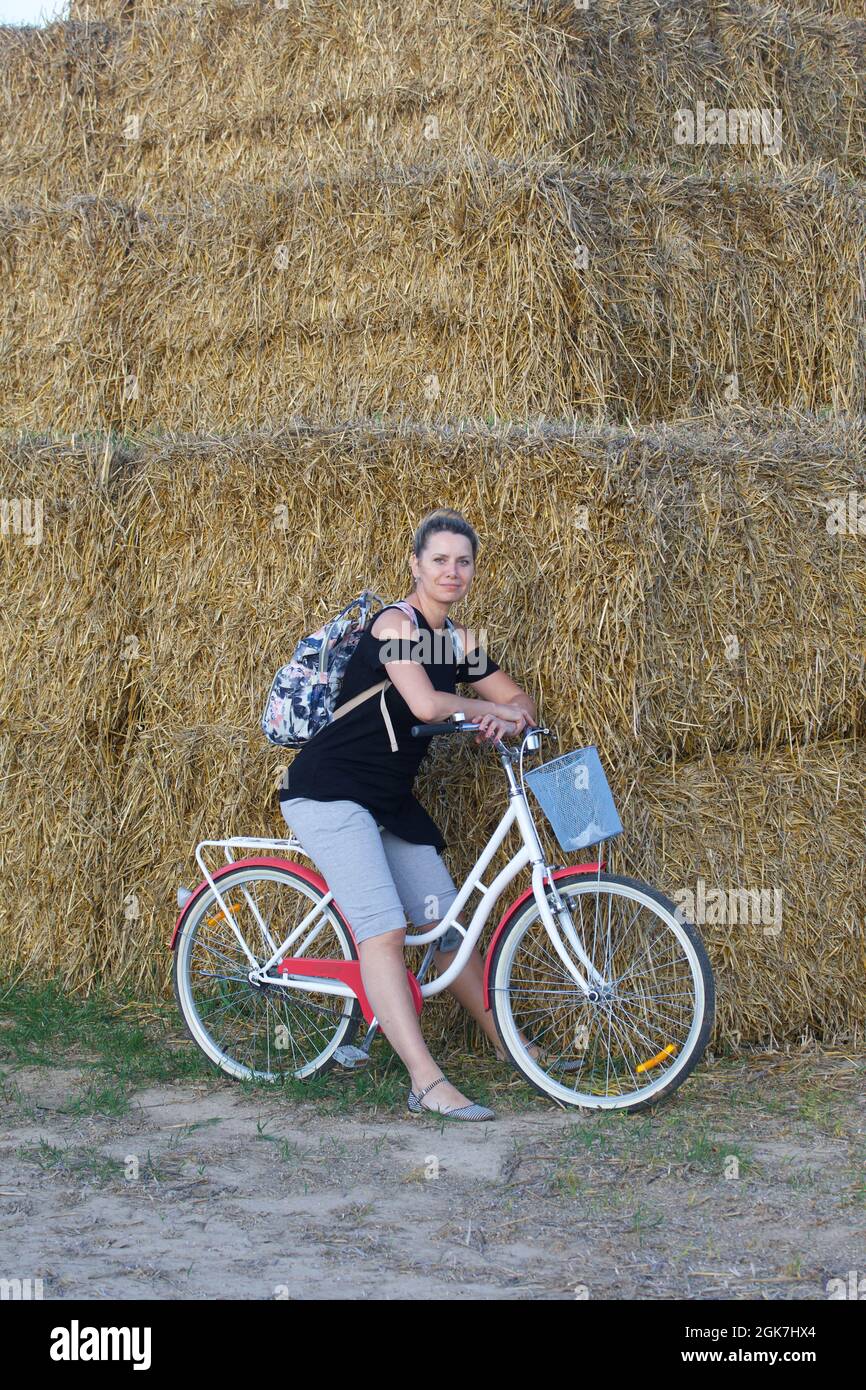 Girl posing near a stack of straw. Sits on a bike. Straw rolls, stacked ...