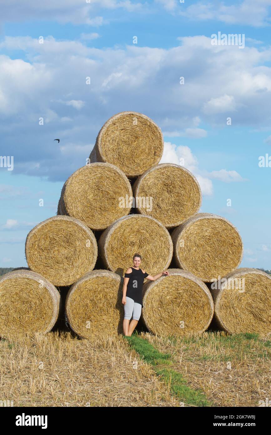Girl posing near a stack of straw. Straw rolls, stacked in a pyramid ...