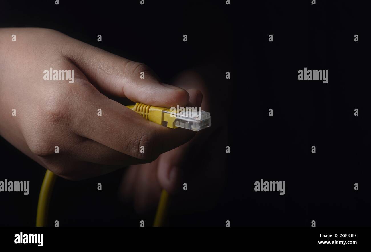 Front Hand holding a Yellow LAN Ethernet cable, and back hand out of ...