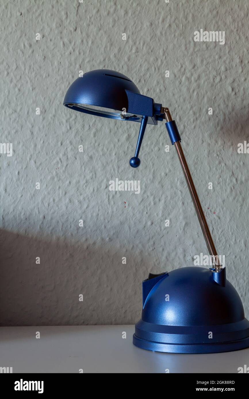 Blue metallic table lamp on a table against a white textured wall Stock ...