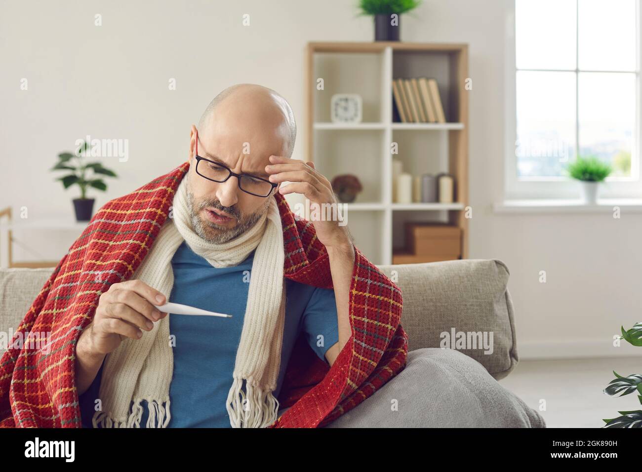 Sick man who has cold or flu fever takes his temperature and looks at ...