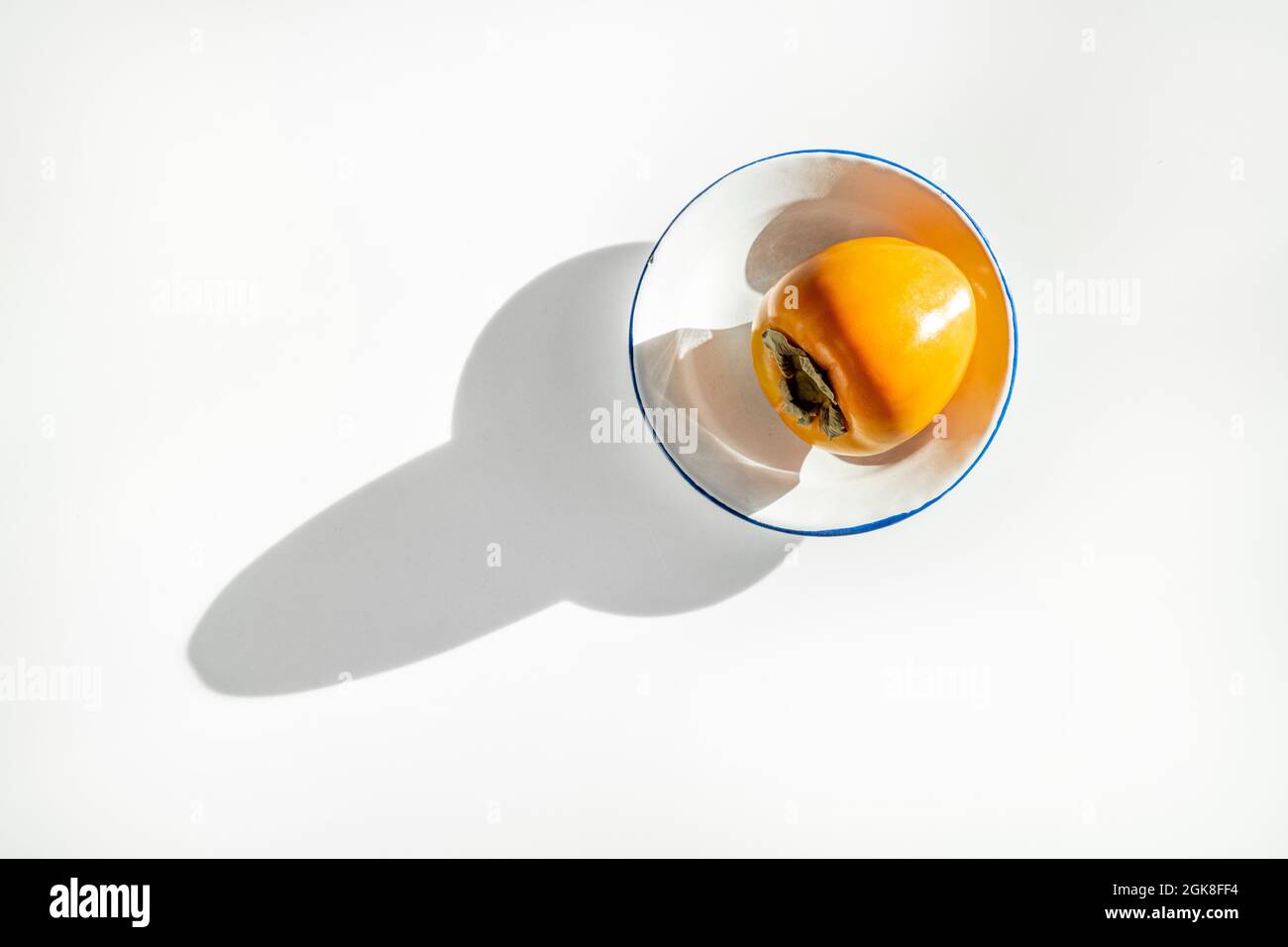 Ripe persimmon on white plate and long shadow on white table Stock ...