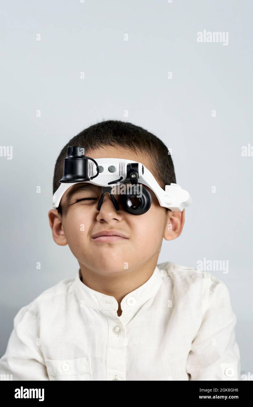Portrait of a cute boy looking through magnifying eyeglasses and making ...