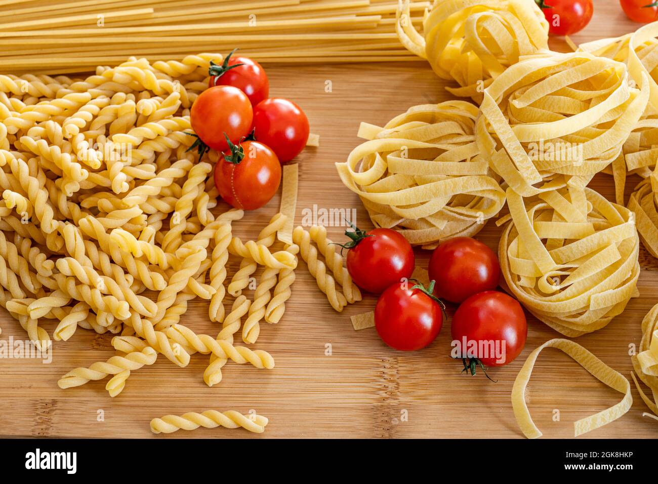Various types of raw Italian wheat flour pasta with cherry tomatoes on ...