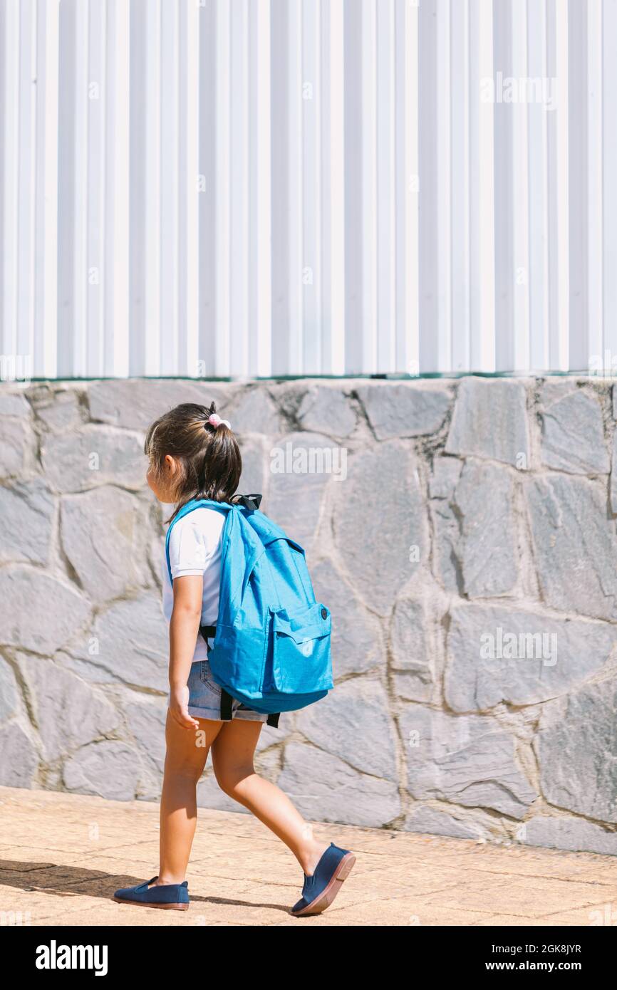 Side view of schoolchild with backpack on pavement looking forward in ...