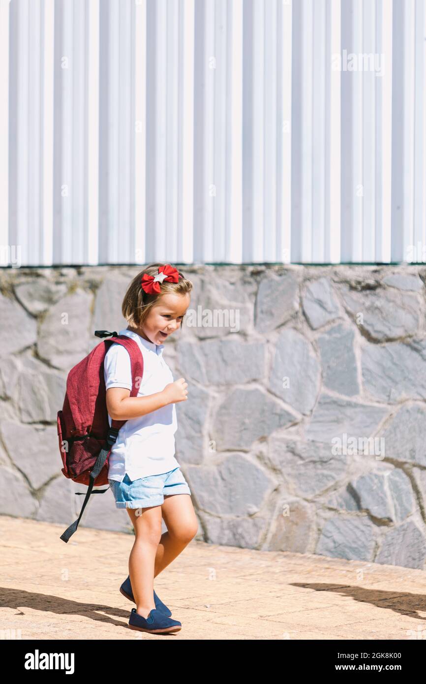 Side view of schoolchild with backpack on pavement looking forward in ...