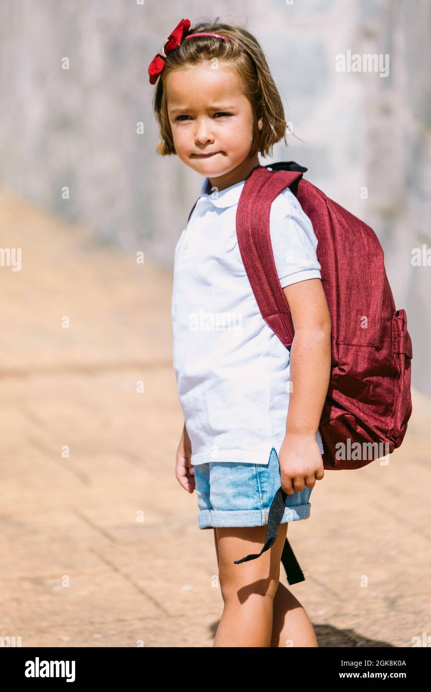 Side view of schoolchild with backpack on pavement looking at camera in ...