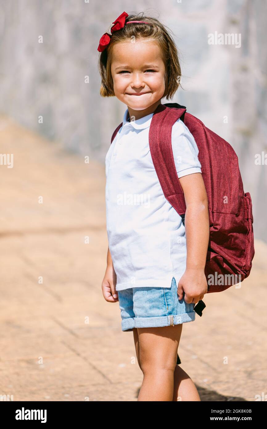 Side view of schoolchild with backpack on pavement looking at camera in ...