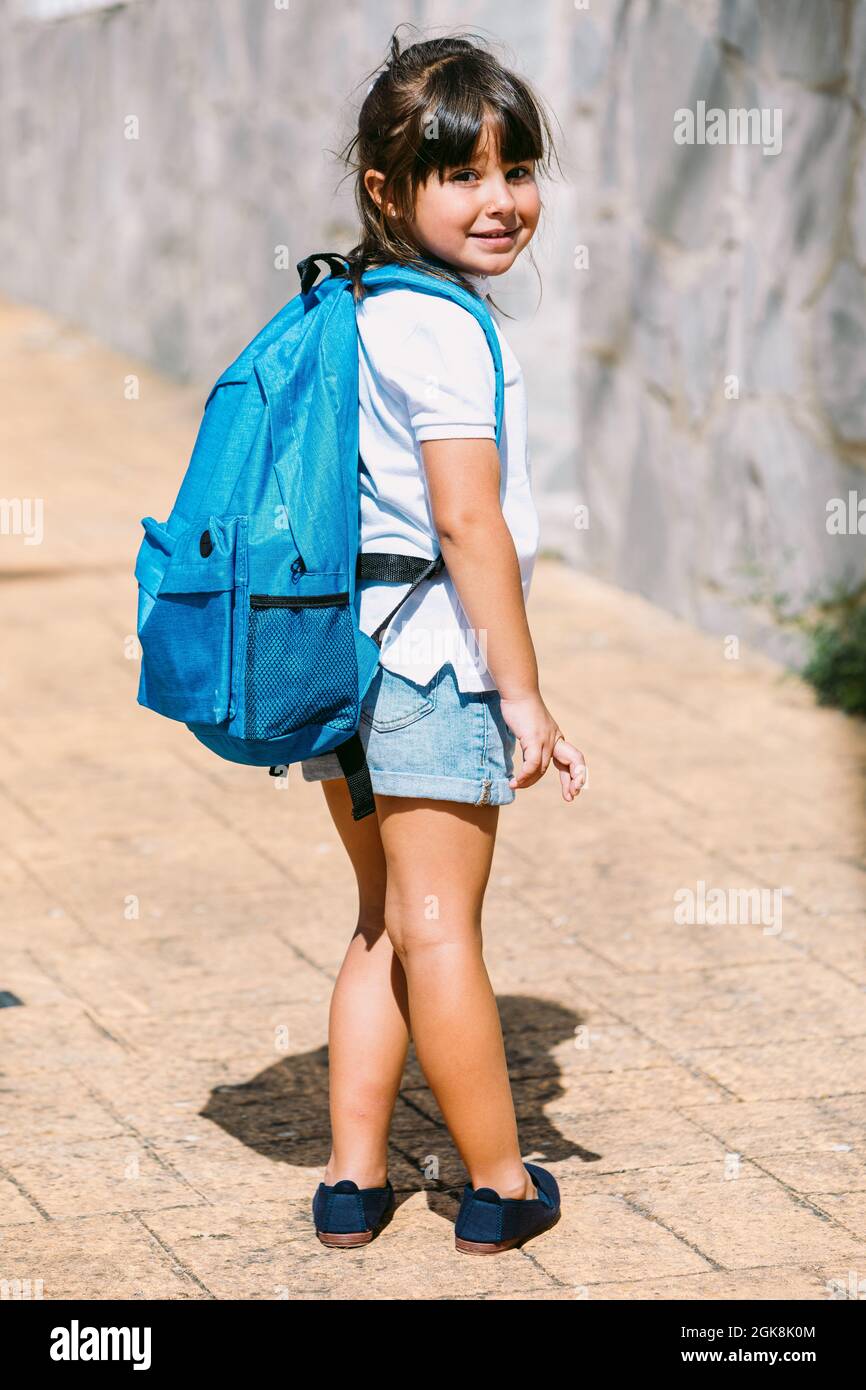 Back view of schoolchild with backpack on pavement looking at camera ...