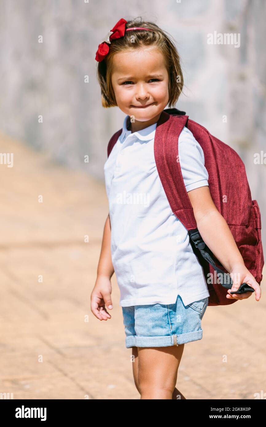 Side view of schoolchild with backpack on pavement looking at camera in ...