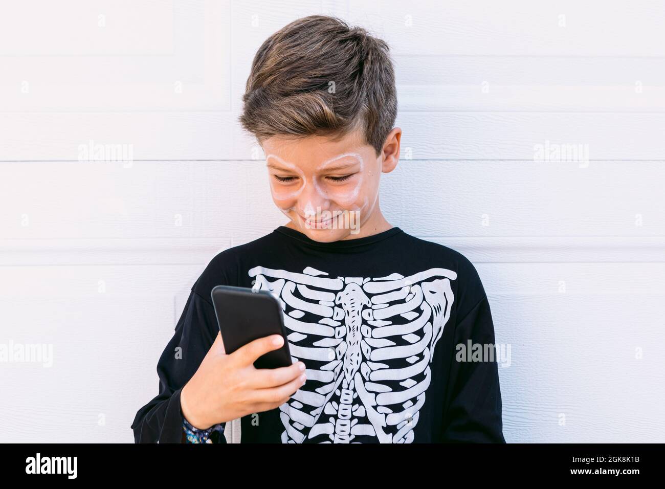 Cheerful boy in black skeleton costume with painted face using on ...