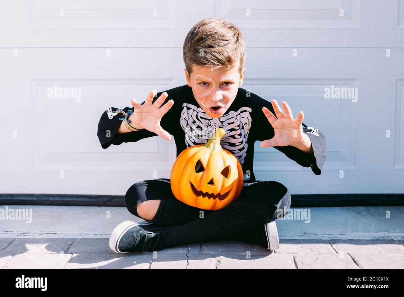 Full body of boy in skeleton costume with Jack o Lantern making evil ...