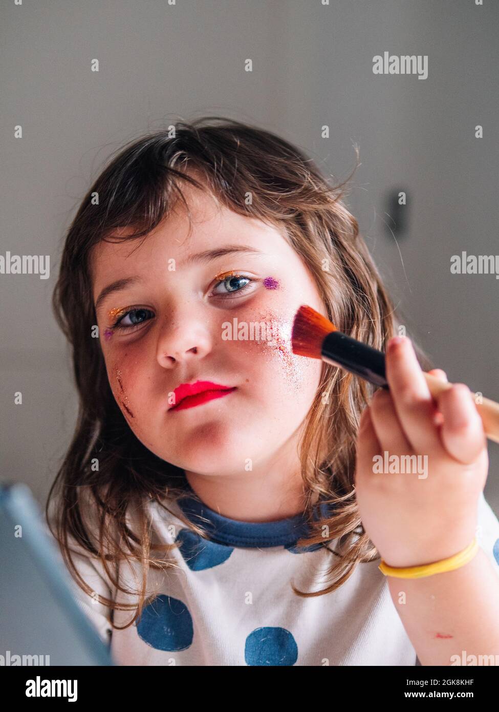 Kid with applicator making up face with assorted cosmetic products in ...