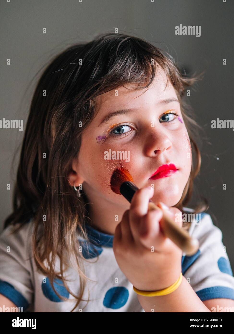 Kid with applicator making up face with assorted cosmetic products in ...