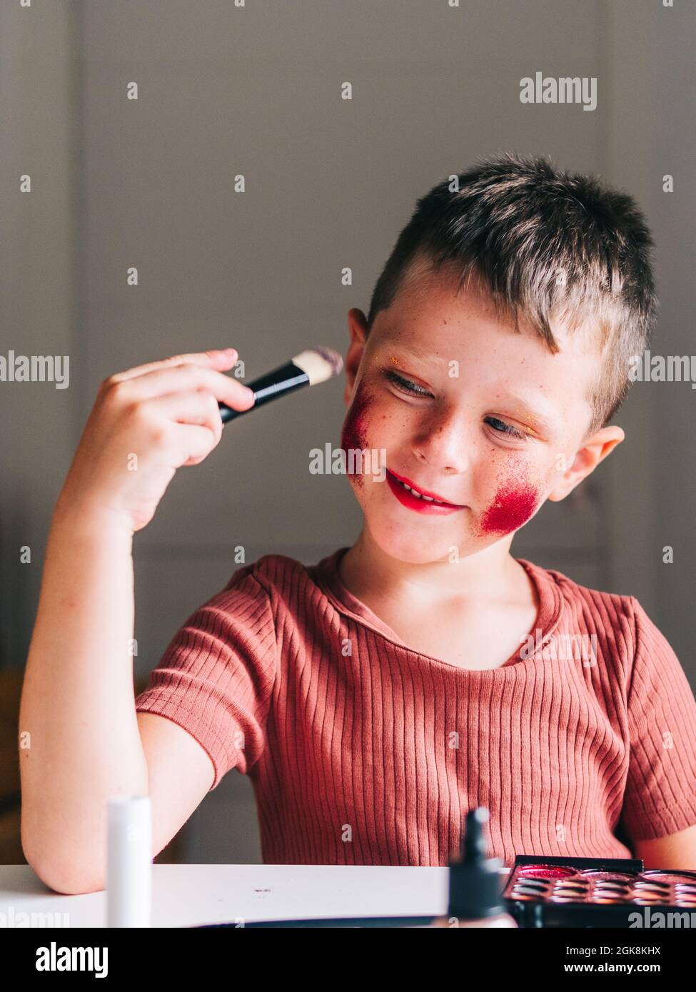 Charming child with makeup applicator looking away at table with ...