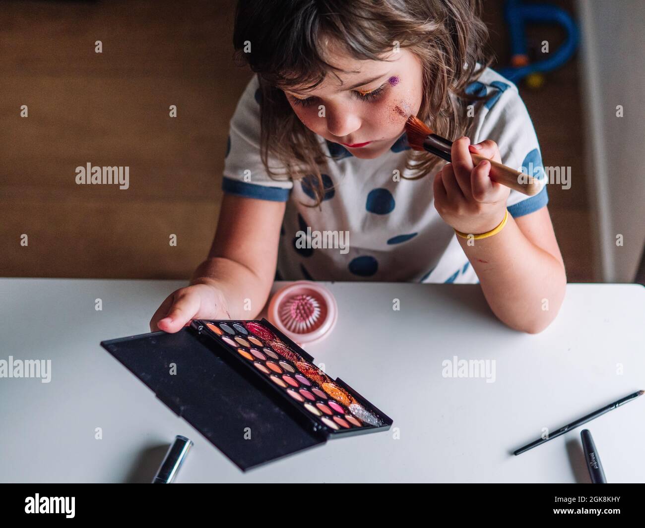From above kid with applicator making up face at table with assorted ...