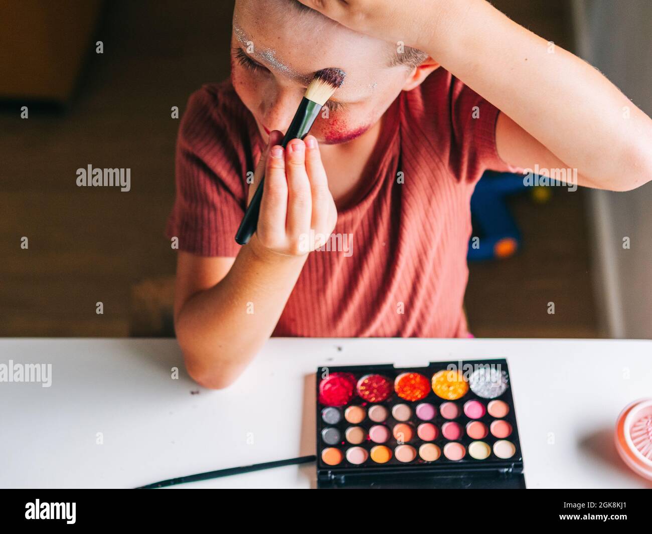 Charming child with makeup applicator touching head while looking away ...