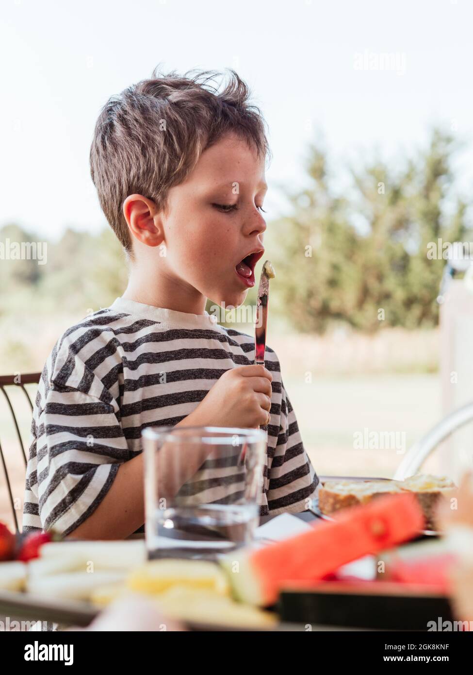 Focused adorable child smearing butter on slice of bread while having ...