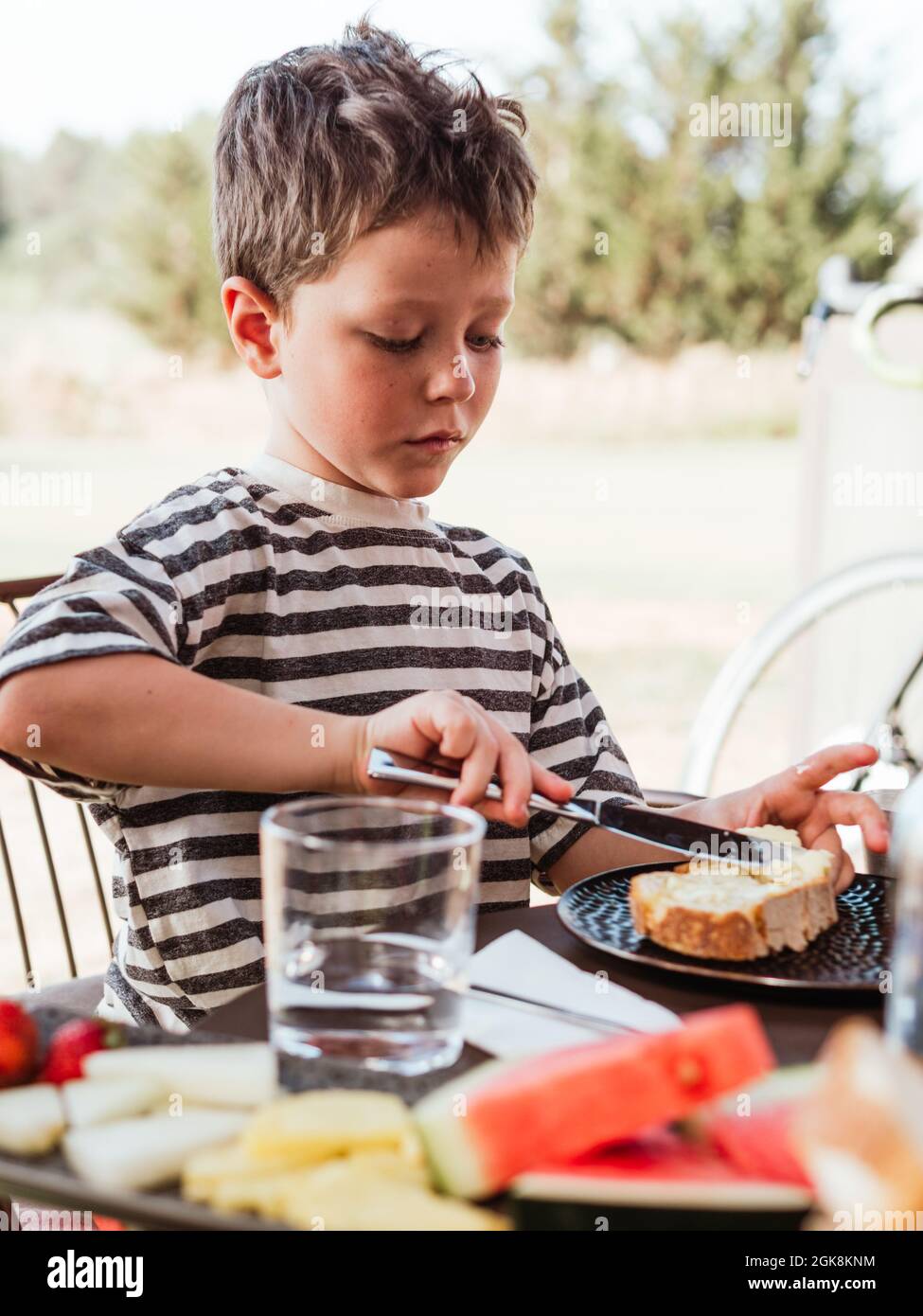 Focused adorable child smearing butter on slice of bread while having ...