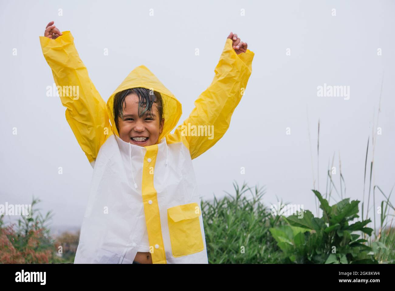 Content Asian child in slicker looking at camera with raised arms while ...