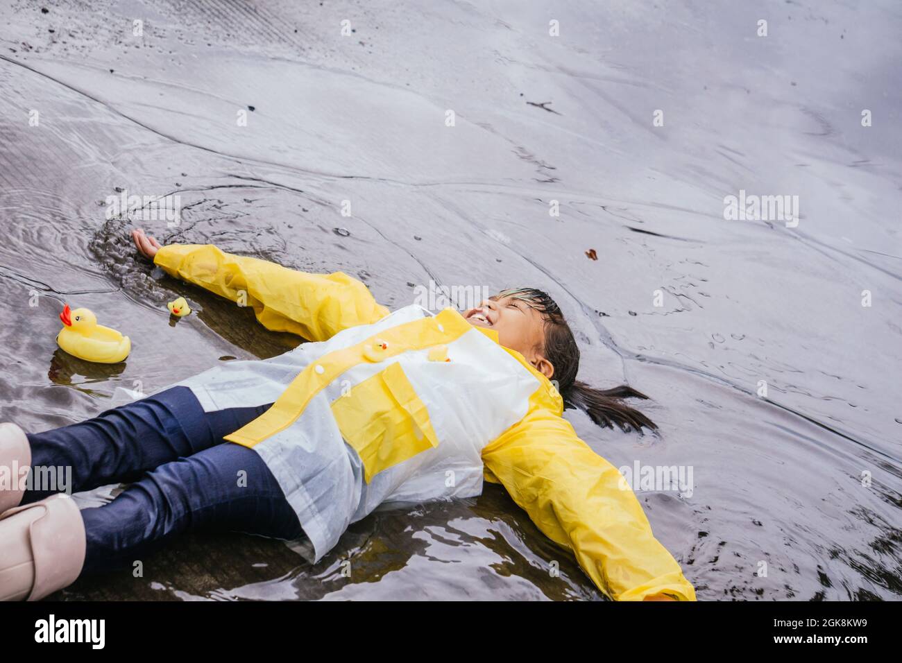 High angle of content Asian kid in rubber boots and slicker lying in ...