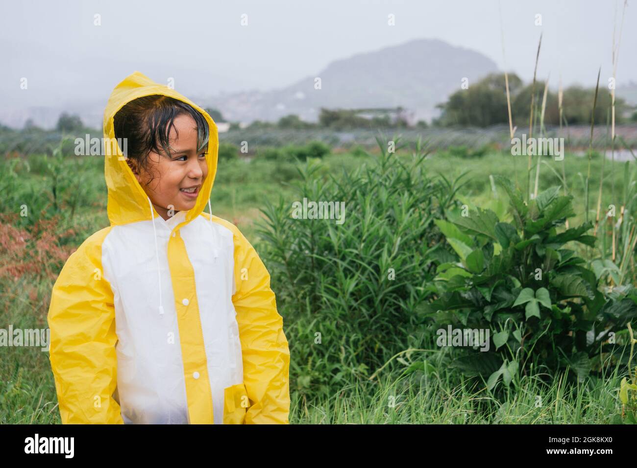 Charming ethnic child in slicker looking away against tropical plants ...