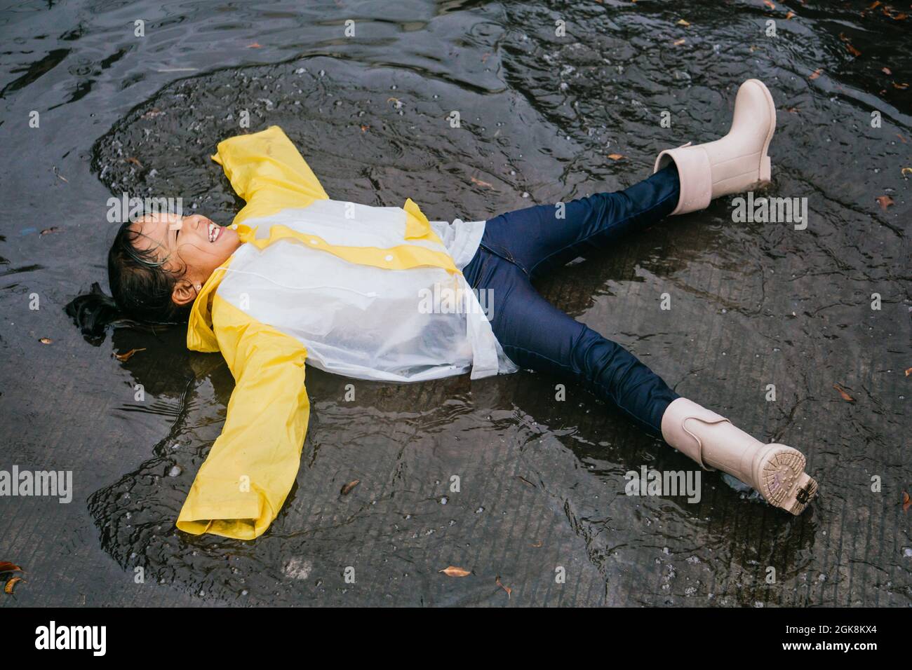 High angle of content Asian kid in rubber boots and slicker lying in ...