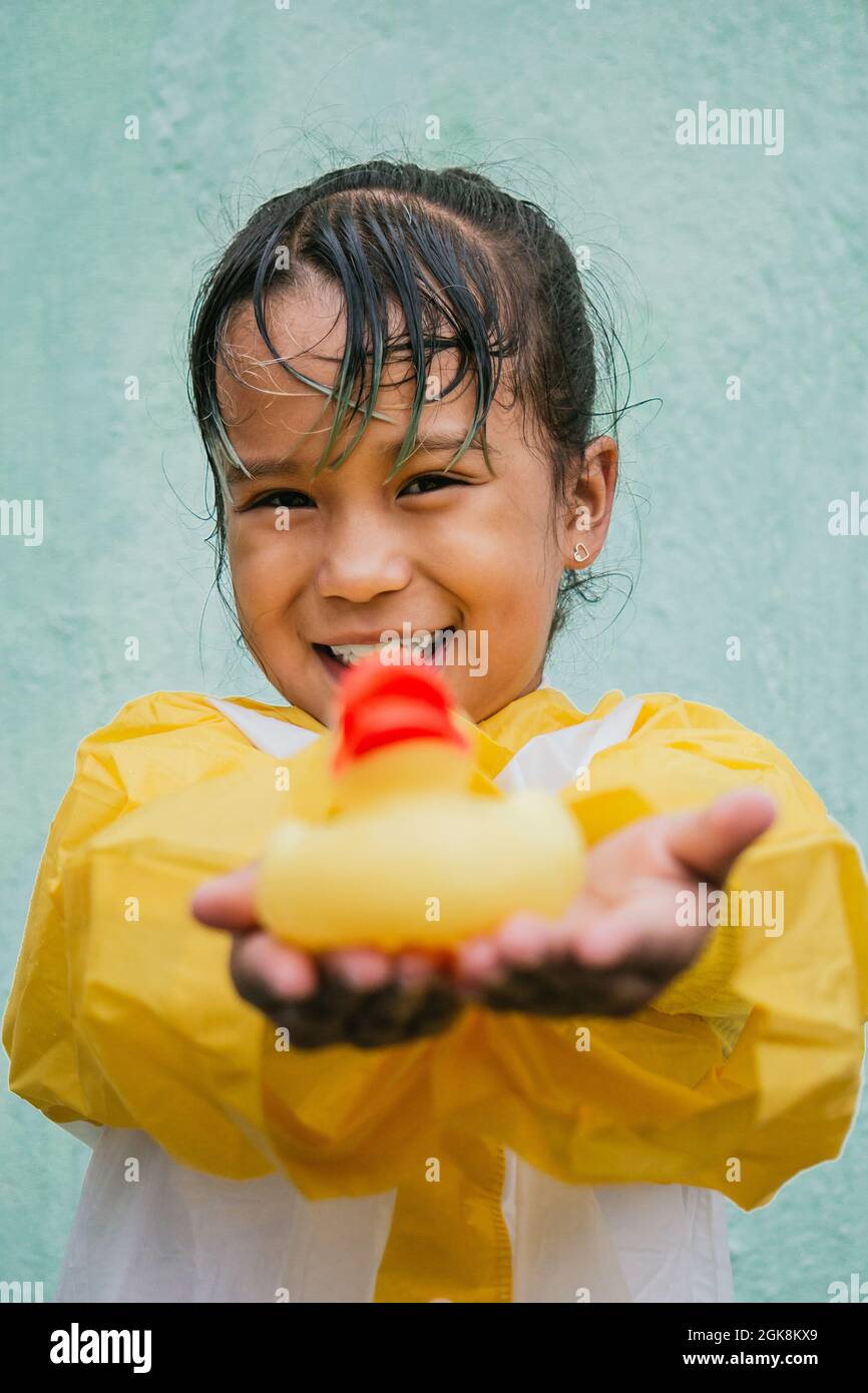 Cheerful ethnic kid in slicker with wet hair and rubber duck looking at ...