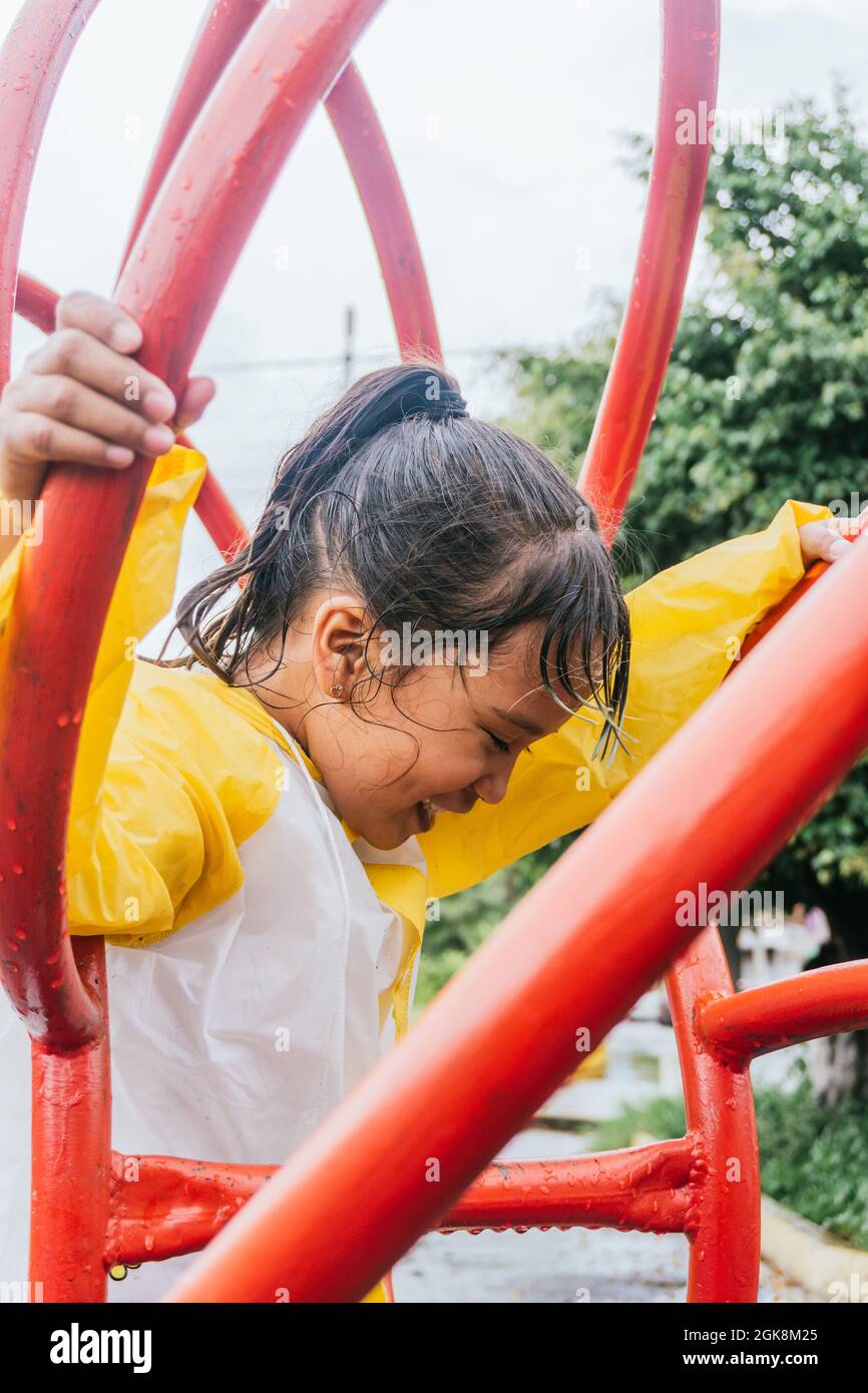 Side view of cheerful ethnic child with wet hair in slicker having fun ...
