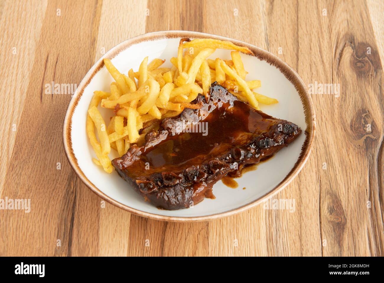 Pork ribs marinated in barbecue sauce with a garnish of fried potatoes ...