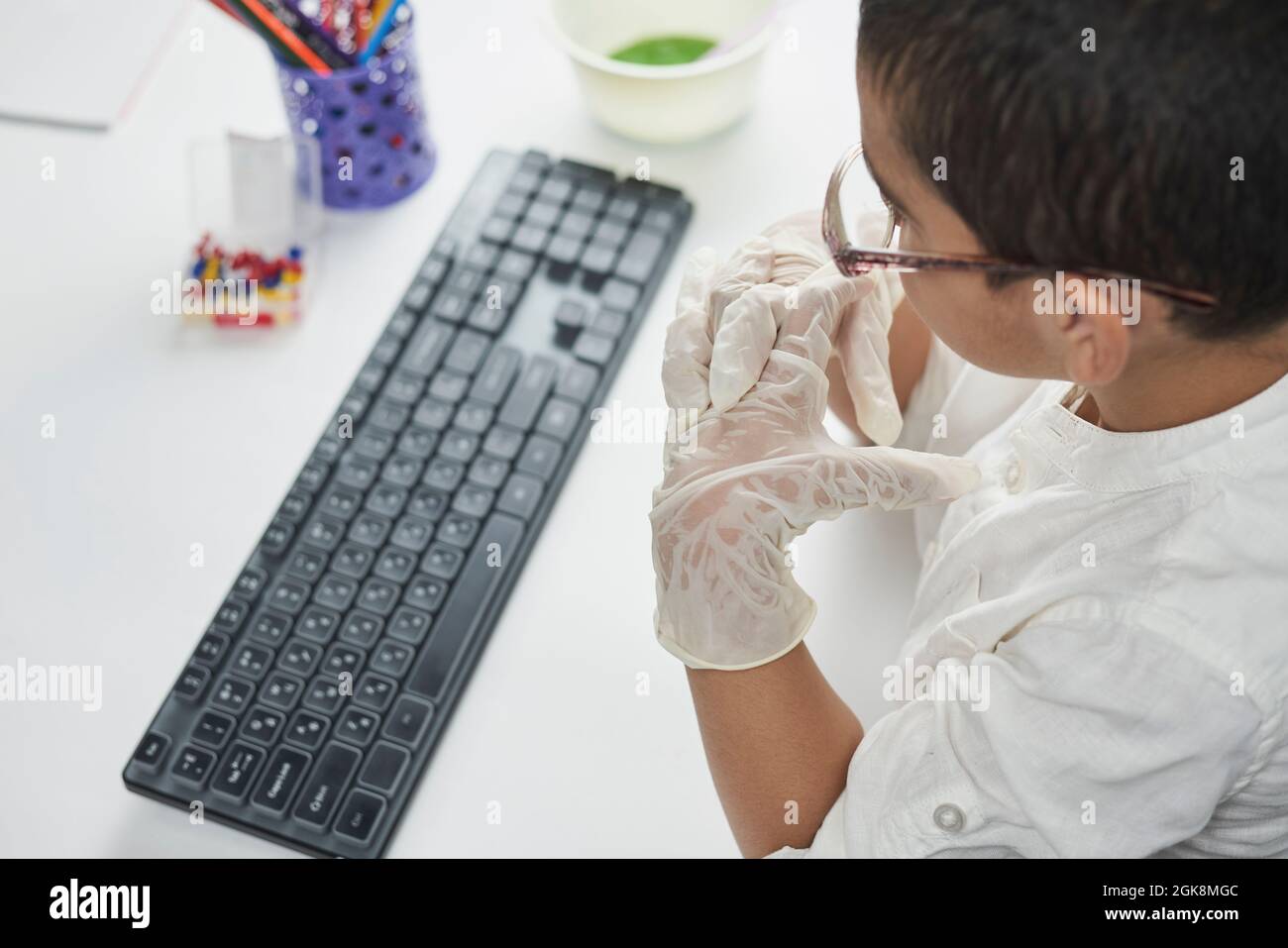 A little kid in gloves and nerd eyeglasses doing his homework online ...
