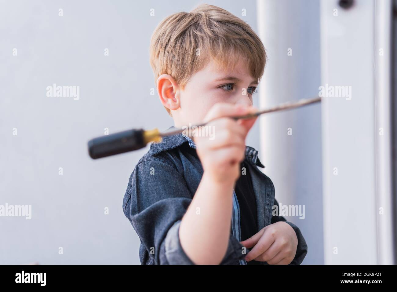 Side view of focused child learning how to use screwdriver in window in ...