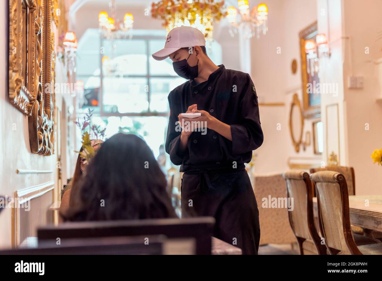 Cafeteria employee in uniform and cloth face mask taking notes of order ...