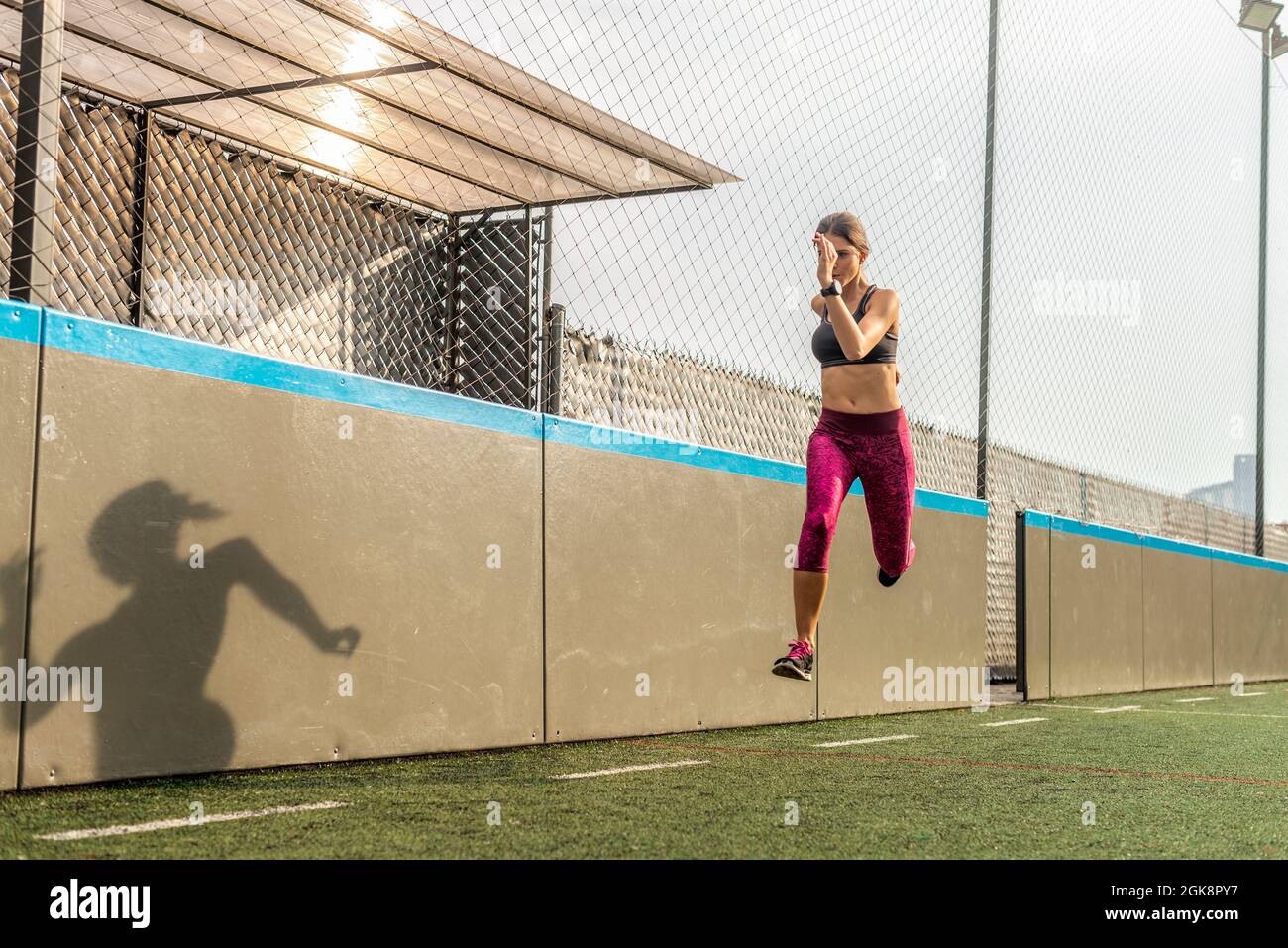 Full body of enduring female athlete in activewear jumping above ground ...