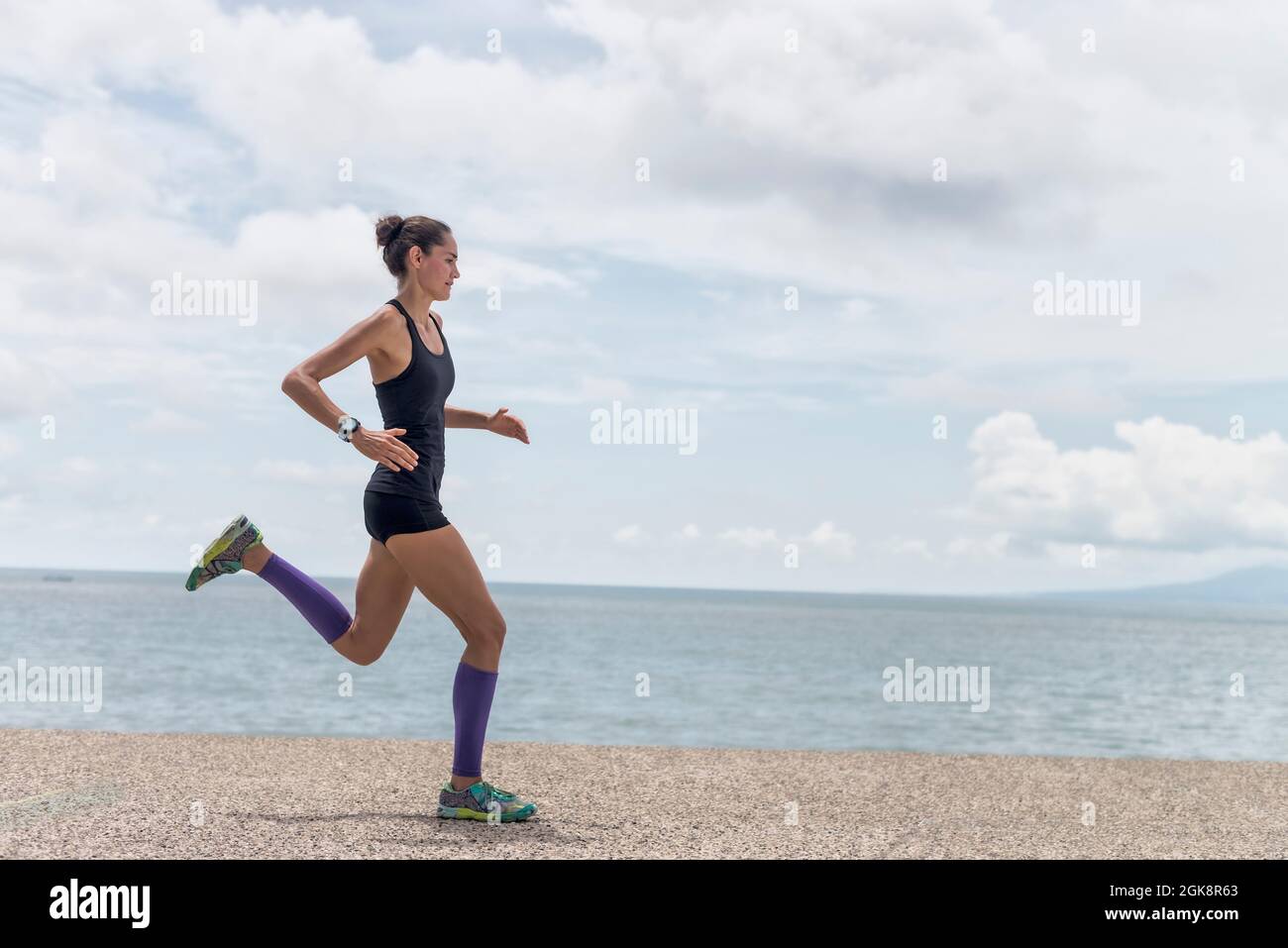 Side view of fit female runner in moment of jumping over promenade ...