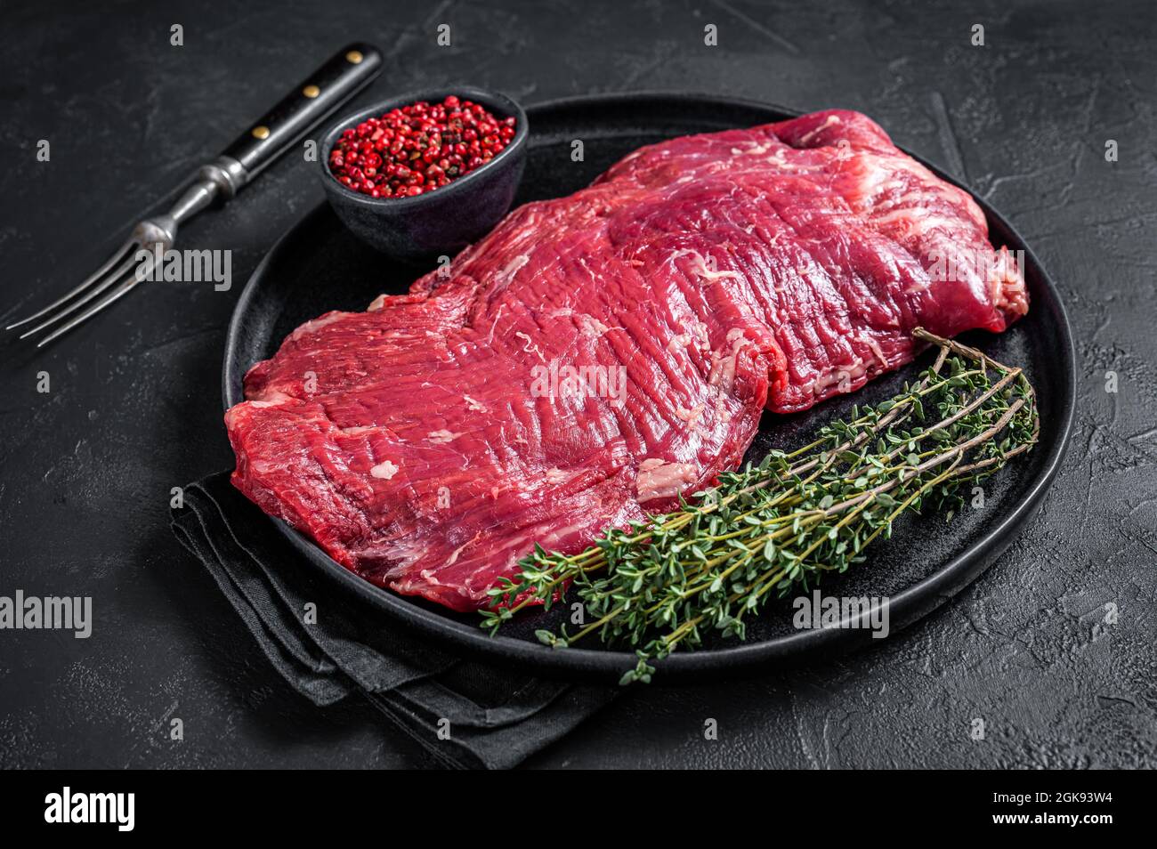 Flank or flap raw beef steak on plate with thyme. Black background. Top ...
