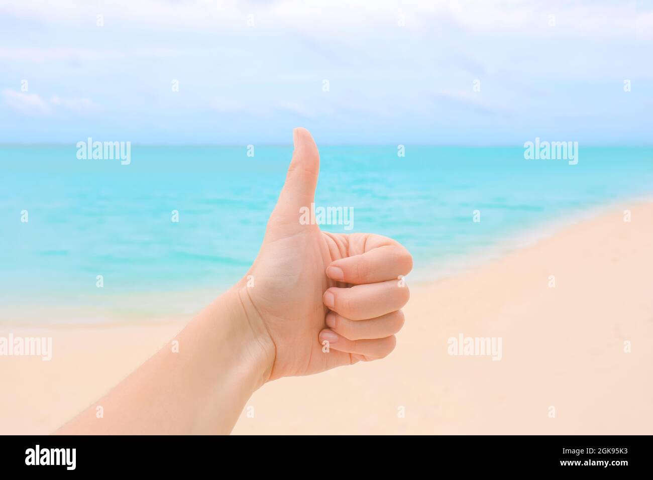 Female hand showing thumb up sign and blurred sea beach on background ...